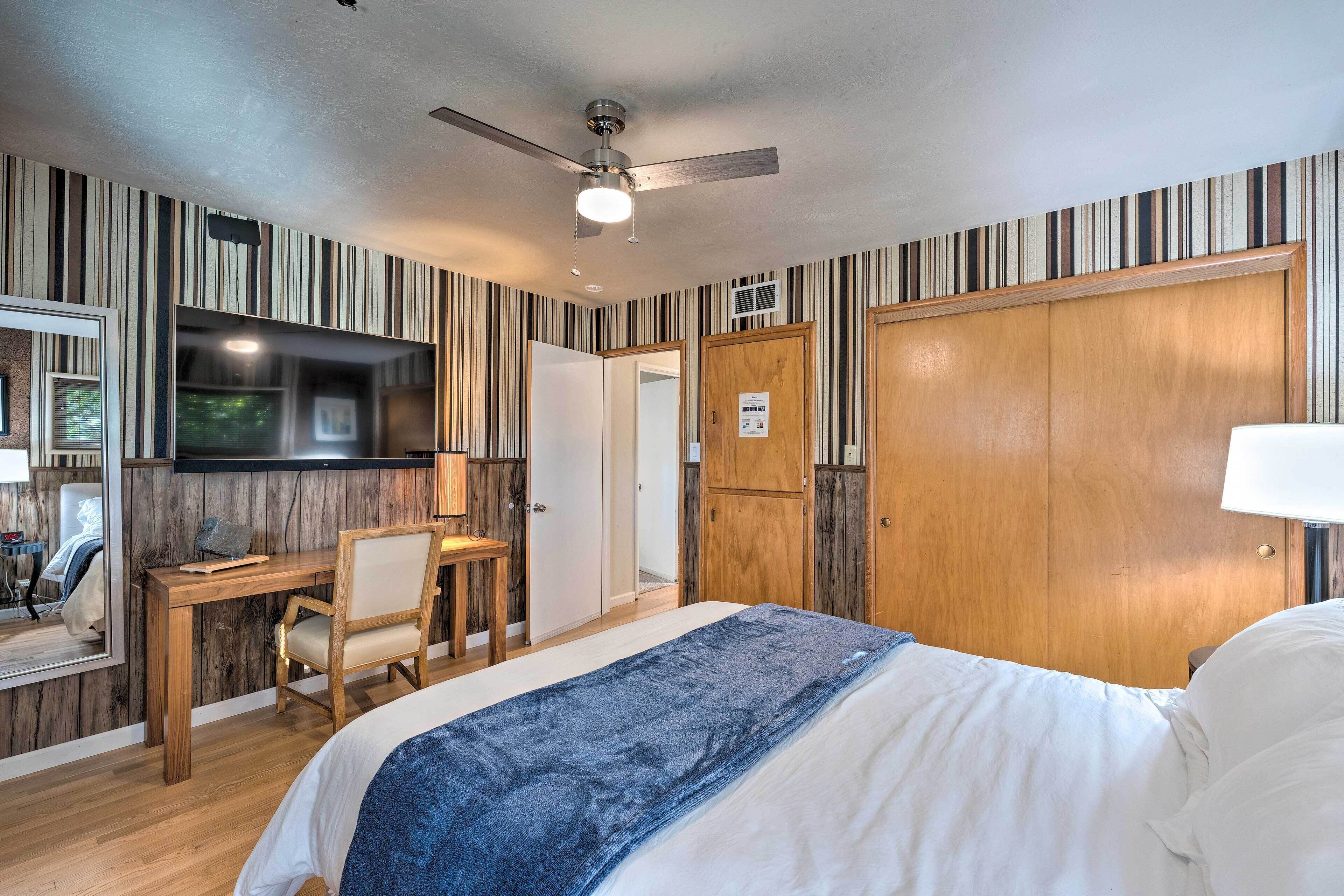 Quarto de hotel com cama, escrivaninha, cadeira, televisão e guarda-roupa.