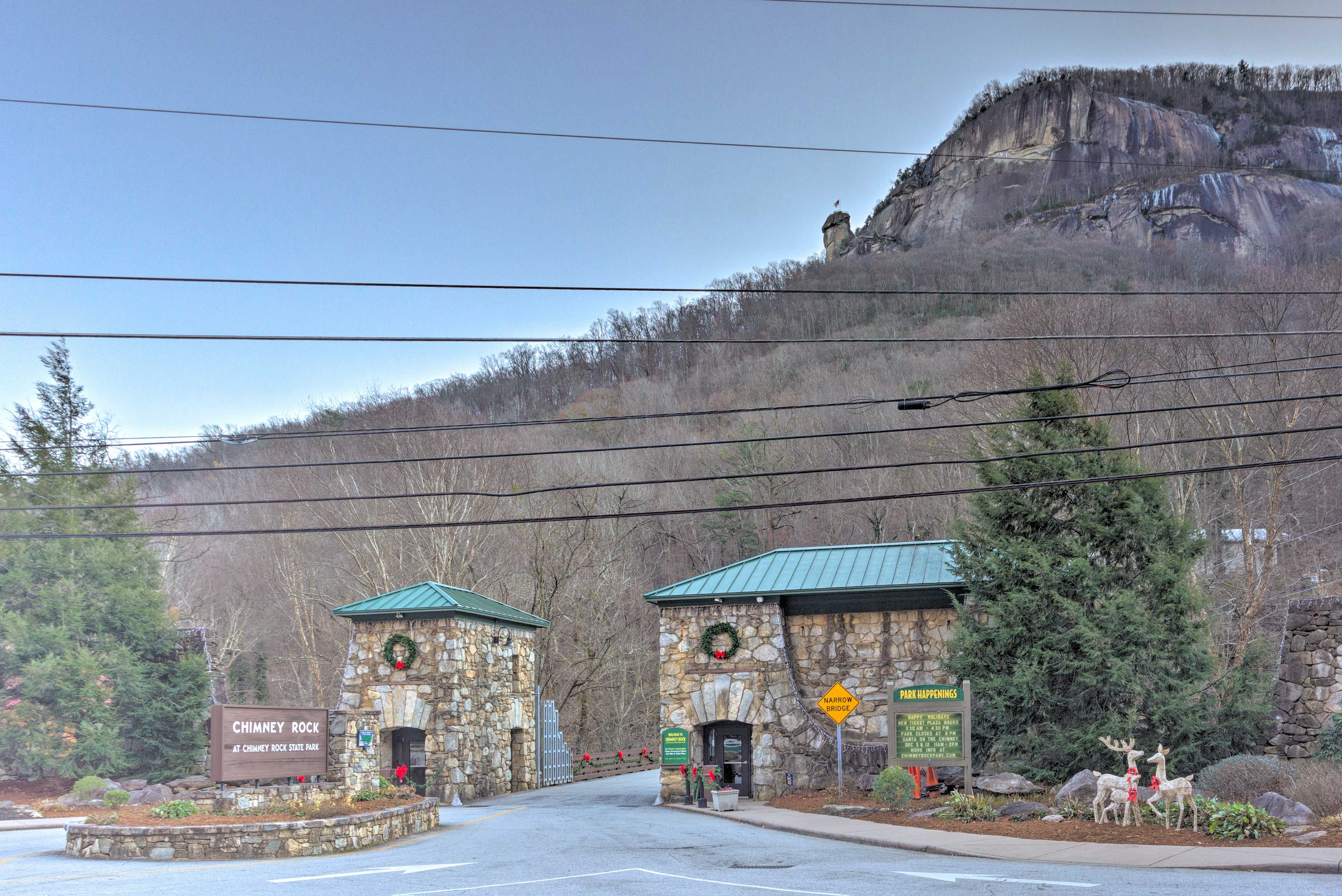 Um edifício de pedra com telhado verde, uma placa com a inscrição 'CHIMNEY ROCK AT CHIMNEY ROCK STATE PARK' e um aviso de 'NARROW BRIDGE'.