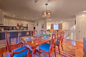 Uma sala de jantar com uma mesa de madeira posta para seis pessoas, rodeada por cadeiras com almofadas azuis.