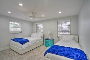 Quarto com duas camas, ventoinha no teto e janelas com cortinas.