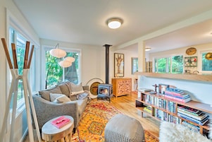 Uma sala de estar aconchegante com lareira, estante de livros e uma grande janela com vista para o verde.