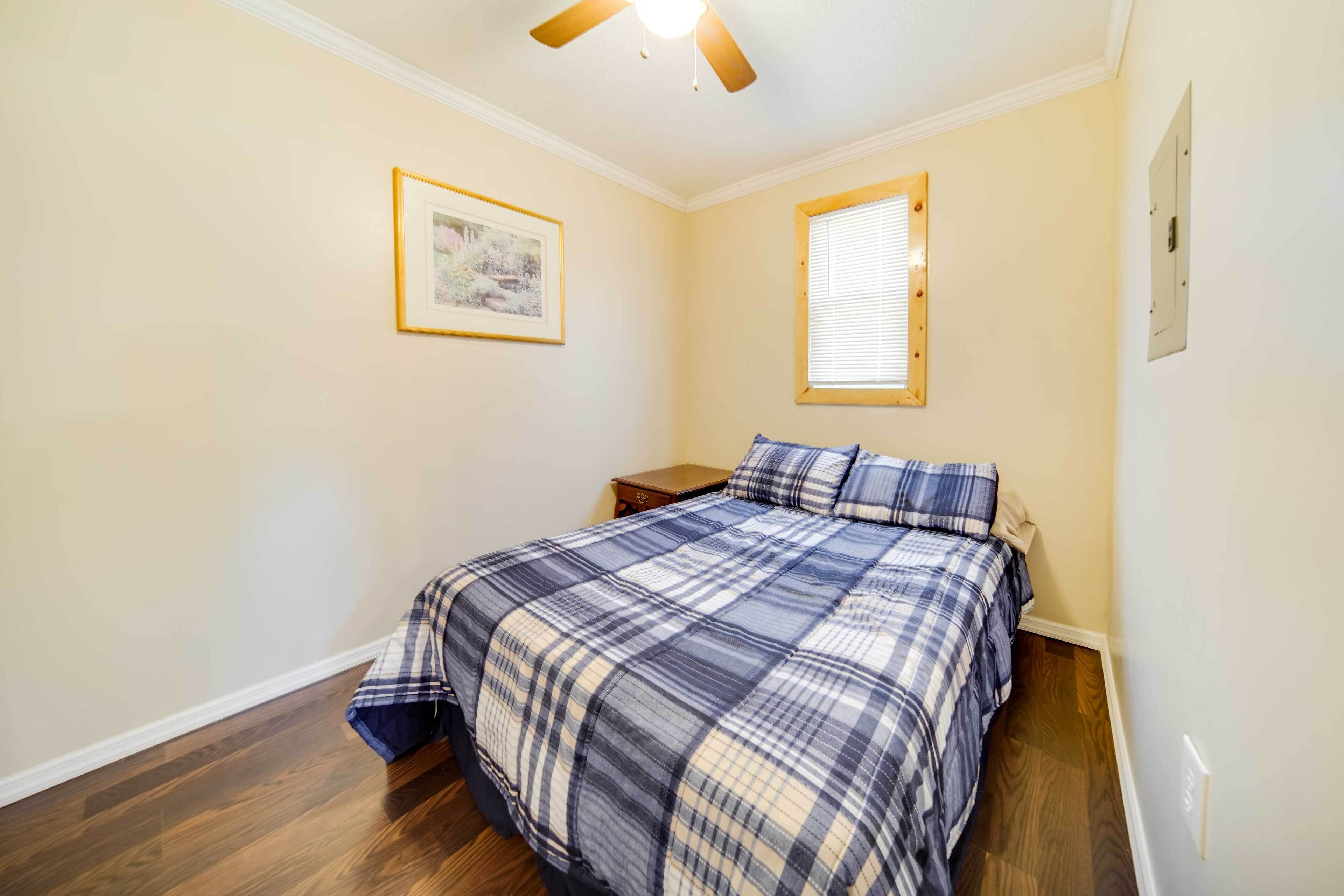 Quarto com cama, mesa de cabeceira, ventilador de teto, janela com persianas e interruptor de luz na parede.