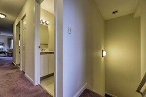 Um corredor com piso coberto por carpete, um interruptor de luz e um luminário fixado na parede.