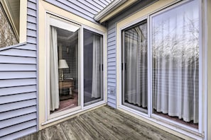 Um deck de madeira com uma porta de vidro deslizante que dá para um quarto com um abajur e uma cadeira.
