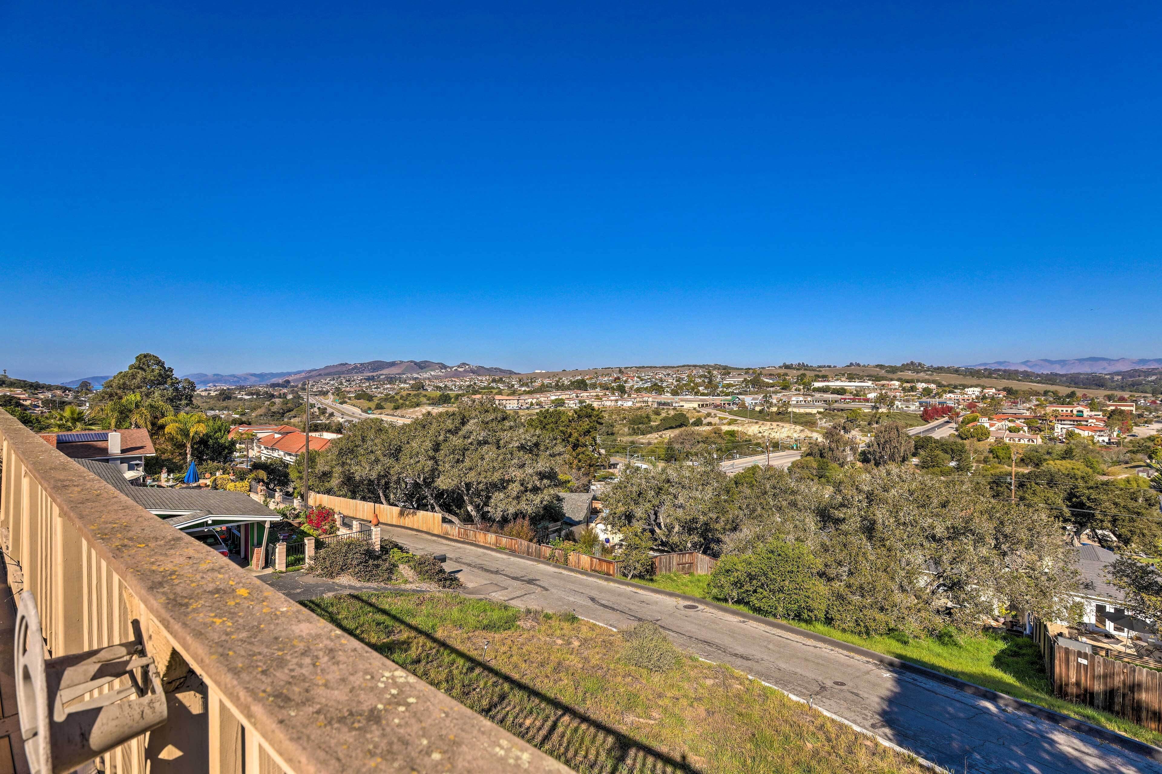 Vista de uma varanda com vista para uma área residencial, com casas, árvores e um céu azul límpido.