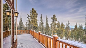 Um deck de madeira com guarda-corpo coberto de neve, que leva a uma área arborizada.