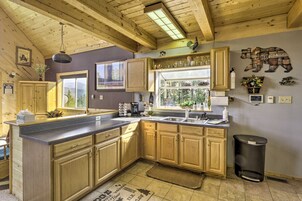 Uma cozinha com armários de madeira, bancada de granito, janela com vista e decoração de parede com tema de urso.
