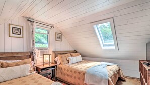 Quarto de sótão acolhedor com duas camas, teto de madeira e claraboia.