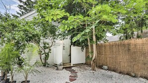 Um jardim com caminho de cascalho, plantas em vasos e cerca de bambu.