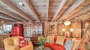 Um interior rústico com teto de madeira, uma geladeira vermelha, um armário de madeira, um sofá com almofadas estampadas e uma pequena mesa redonda com um vaso de flores.