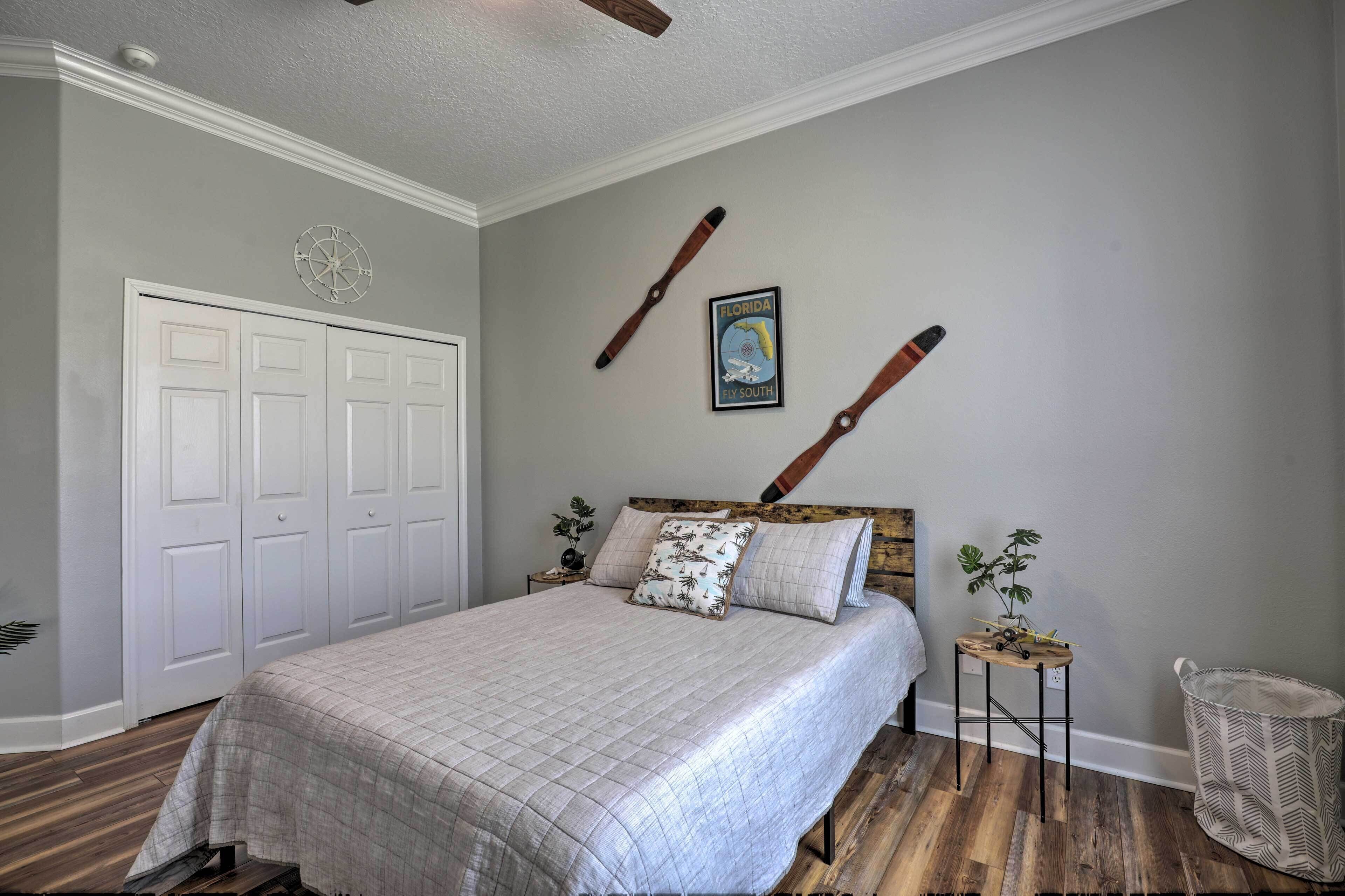 Um quarto com cama, mesa de cabeceira, relógio na parede, pôster emoldurado da Flórida e piso de madeira.