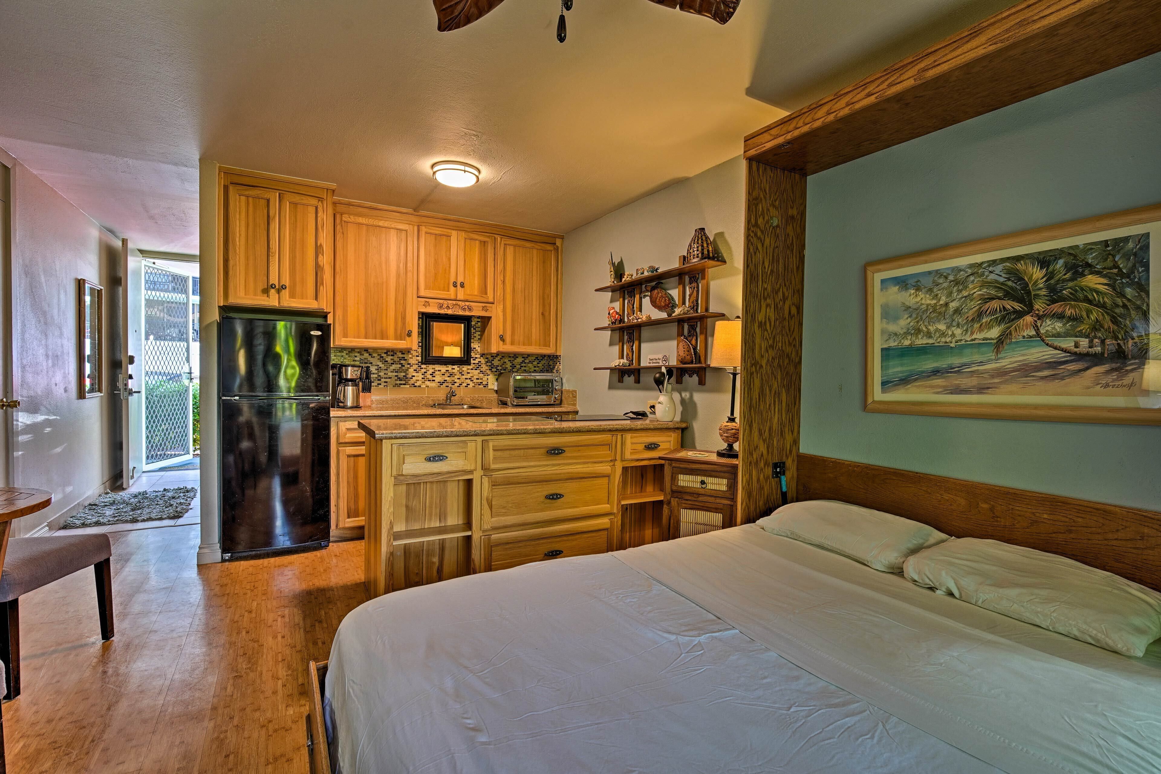 Quarto com cama grande, armários de madeira, geladeira e cozinha equipada com micro-ondas e torradeira.