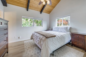 Quarto com cama, mesa de cabeceira, cômoda e duas janelas.