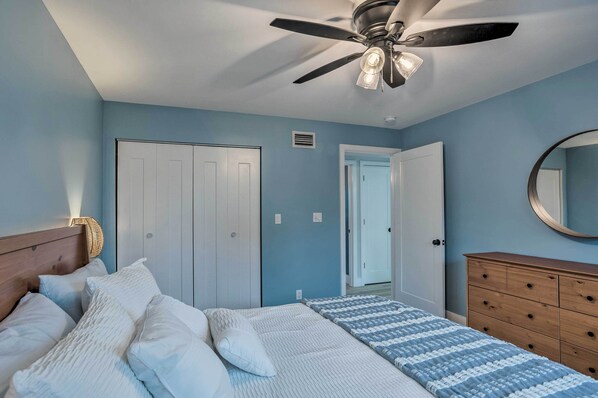 Quarto com uma cama, cômoda, ventilador de teto e porta que dá para outro ambiente.