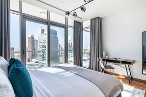 Quarto de hotel moderno com uma cama grande, uma escrivaninha e vista para o horizonte da cidade através de janelas do chão ao teto.