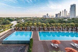 Uma piscina no terraço com duas áreas distintas, rodeada por palmeiras e espreguiçadeiras.