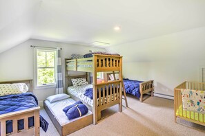 Quarto infantil com beliches, berço e janela com cortinas.
