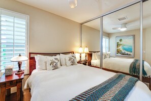 Quarto de hotel com uma cama grande, mesa de cabeceira com abajur, criado-mudo e um espelho, além de um quadro na parede.