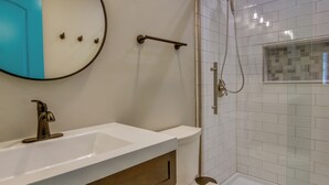 Casa de banho com uma pia branca, um espelho e área de duche com porta de vidro.