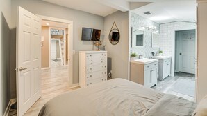 Quarto com cama, cômoda, espelho e televisão.