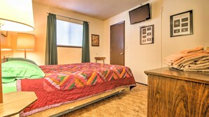 Quarto com cama, escrivaninha, cadeira, televisão e porta.
