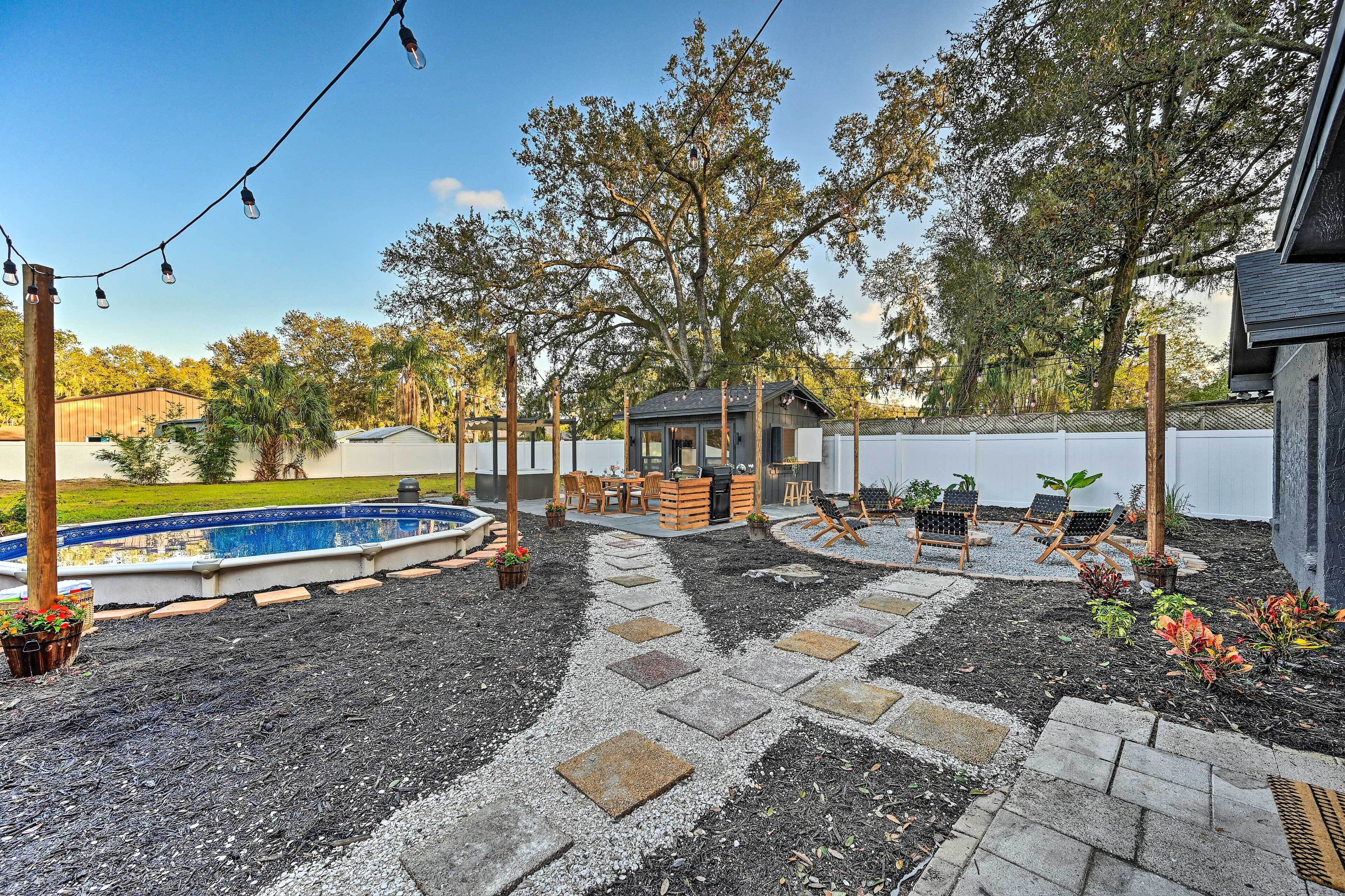 Um quintal com piscina, caminho de pedra, área de estar externa e um pequeno gazebo.