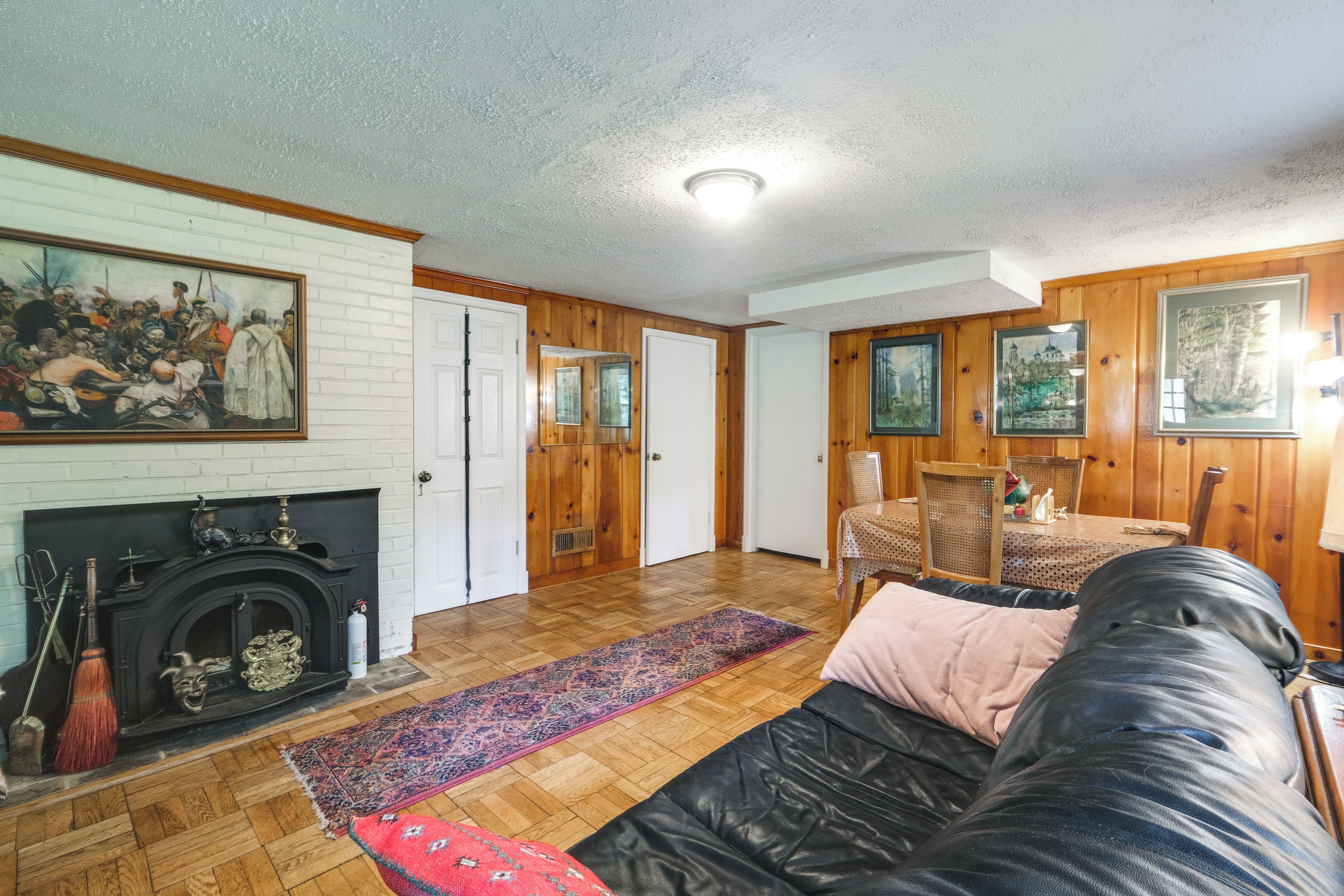 Uma sala de estar com lareira, um sofá de couro preto, um tapete estampado e paredes de madeira.