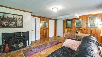 Uma sala de estar com lareira, um sofá de couro preto, um tapete estampado e paredes de madeira.