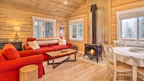 Interior acolhedor de uma cabana com um sofá vermelho, piso de madeira, lareira e grandes janelas com vista para a floresta.
