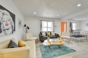 Uma sala moderna com um sofá, poltronas, uma mesa de centro e um espaço de jantar com mesa e cadeiras.