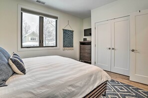 Quarto com cama grande, guarda-roupa, tapeçaria pendurada e janela com vista para uma casa.