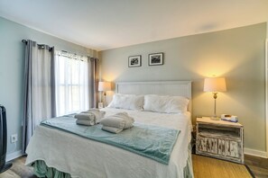 Cama bem arrumada com lençóis brancos e um cobertor verde, duas luminárias de cabeceira e uma mesinha de cabeceira com uma luminária e uma caixa de lenços.