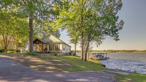 Uma casa à beira do lago com varanda coberta, um cais e um gramado.