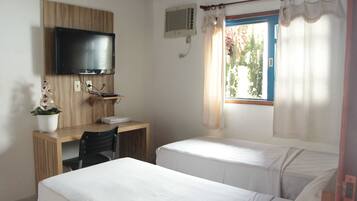 Quarto com duas camas, uma escrivaninha com cadeira, televisão fixada na parede e janela com cortinas.