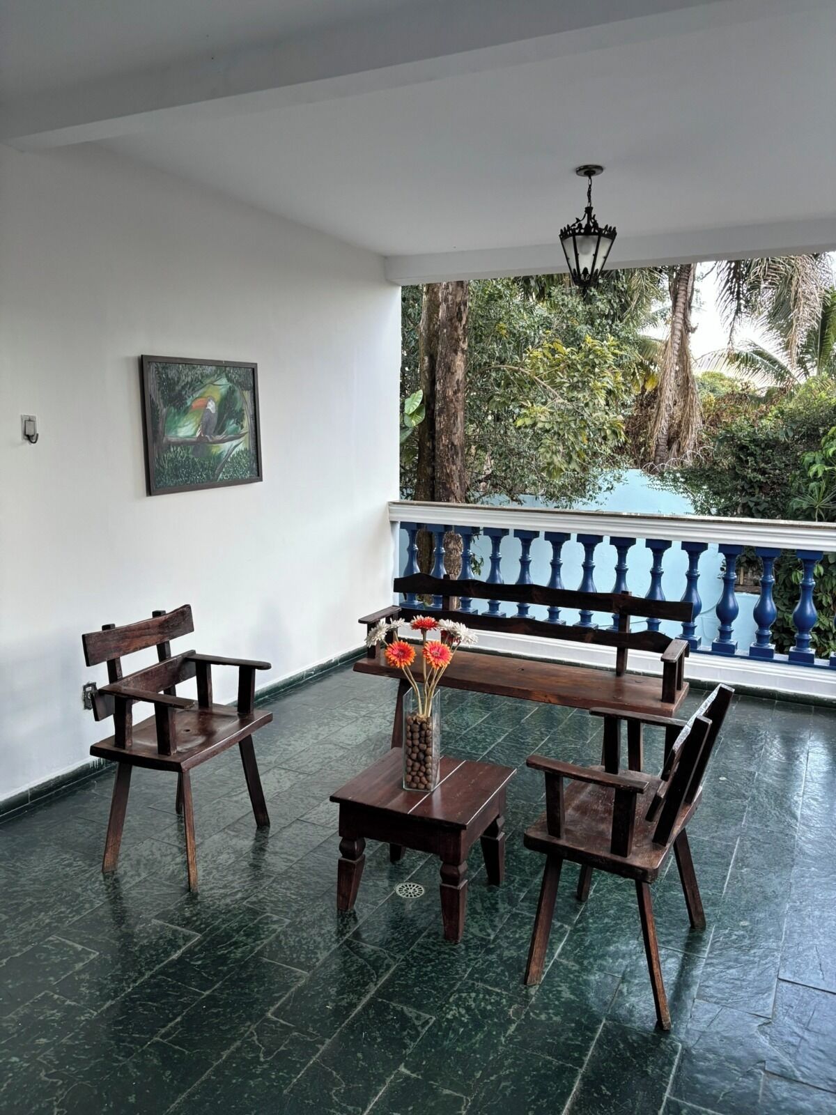 Uma varanda com uma mesa e cadeiras de madeira, um vaso com flores e um quadro na parede.