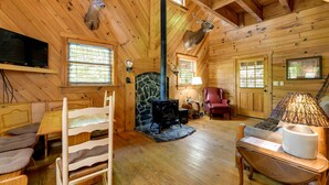 Interior de uma cabana de madeira com lareira de pedra, móveis rústicos e chifres de veado fixados no teto.