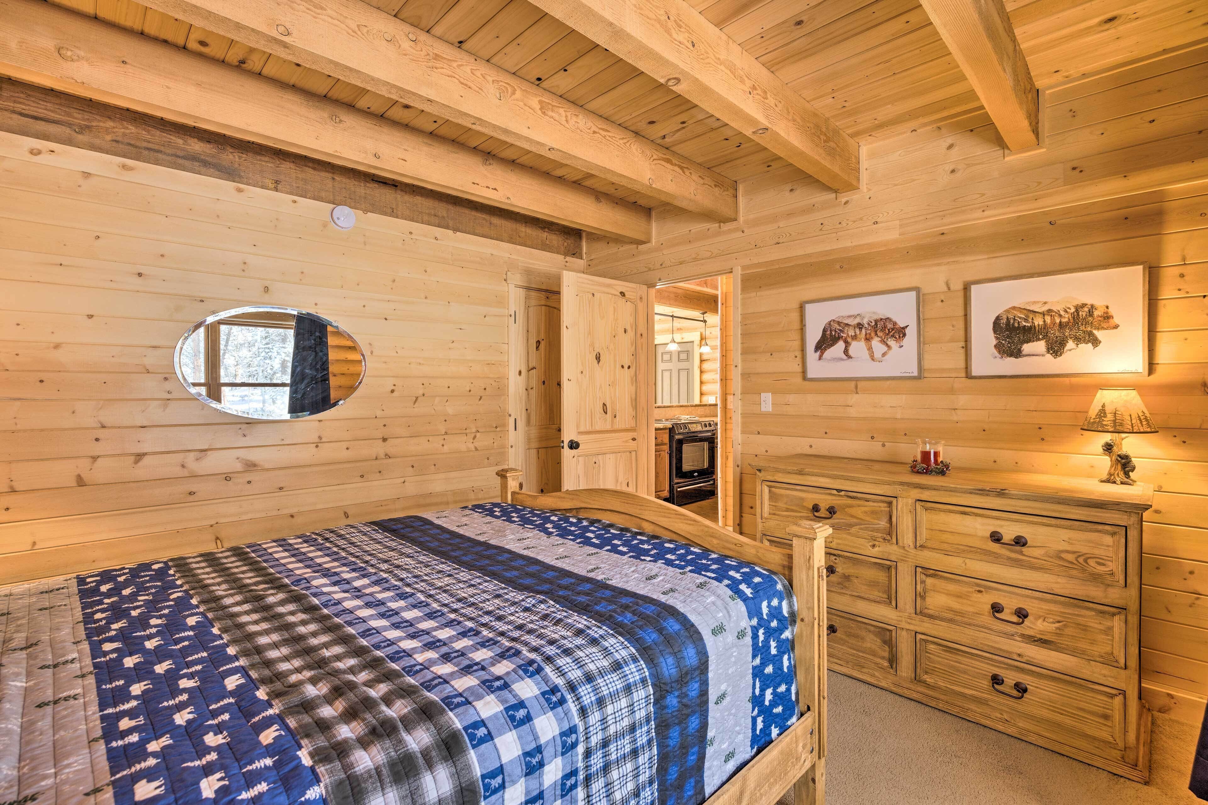 Interior de cabana de madeira com uma cama, cómoda e quadros de animais na parede.