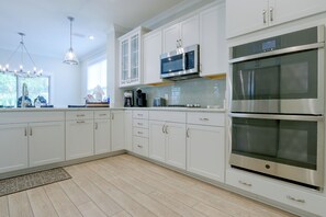 Uma cozinha moderna com armários brancos, eletrodomésticos de aço inoxidável e uma grande janela que oferece luz natural.