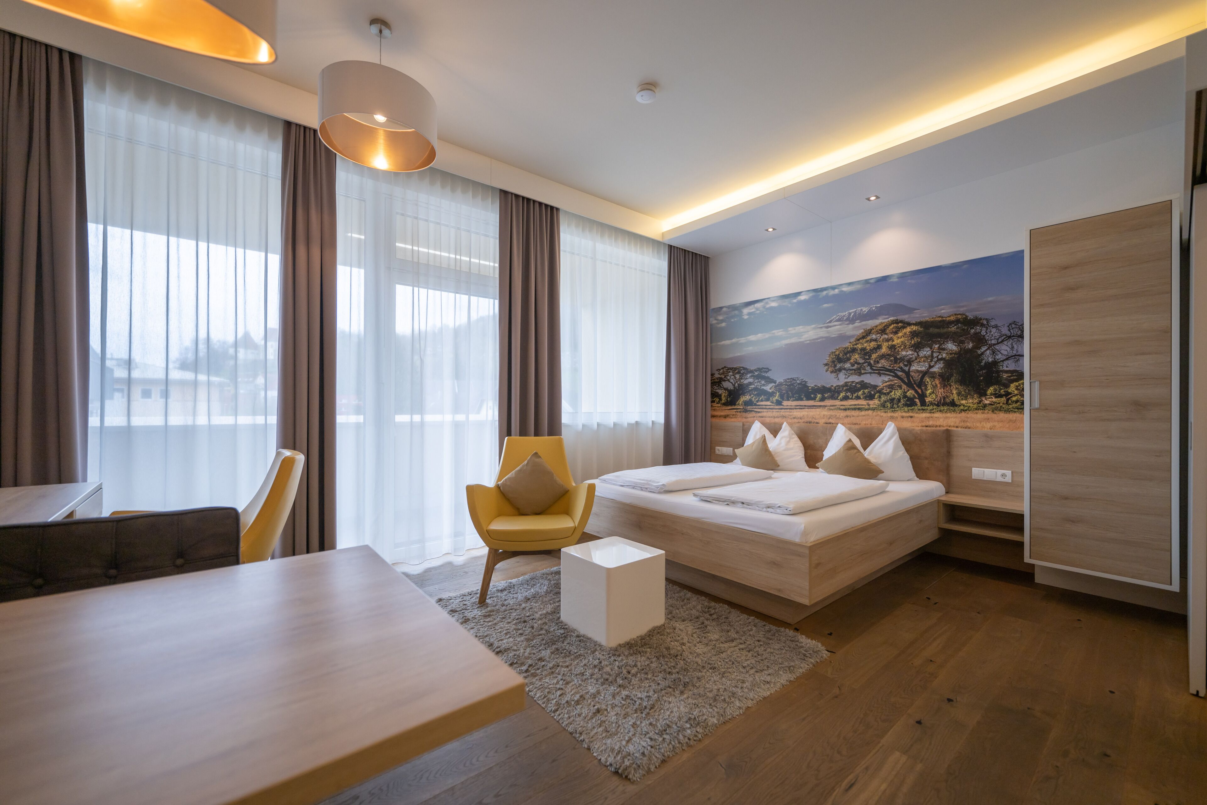 Quarto de hotel moderno com cama de madeira, mesa de jantar e janela grande com cortinas.