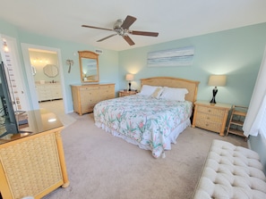 Quarto com cama, duas mesas de cabeceira, ventilador de teto, cômoda, espelho e um quadro na parede.