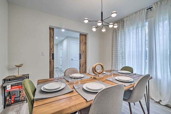 Uma sala de jantar com uma mesa de madeira posta para quatro pessoas, incluindo pratos, copos e um arranjo central.