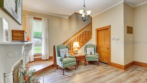 Um quarto com escada de madeira, duas poltronas verdes, uma mesa de madeira com uma luminária e uma lareira.