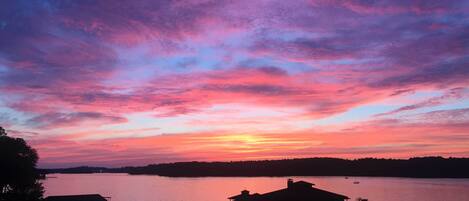Um pôr do sol sobre um lago calmo, com um píer e edifícios na margem.