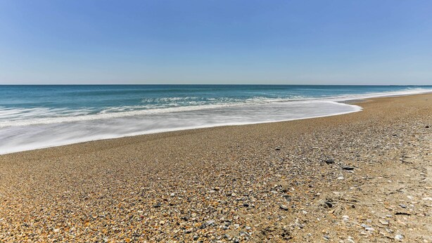 Uma praia de seixos com ondas suaves e céu claro.