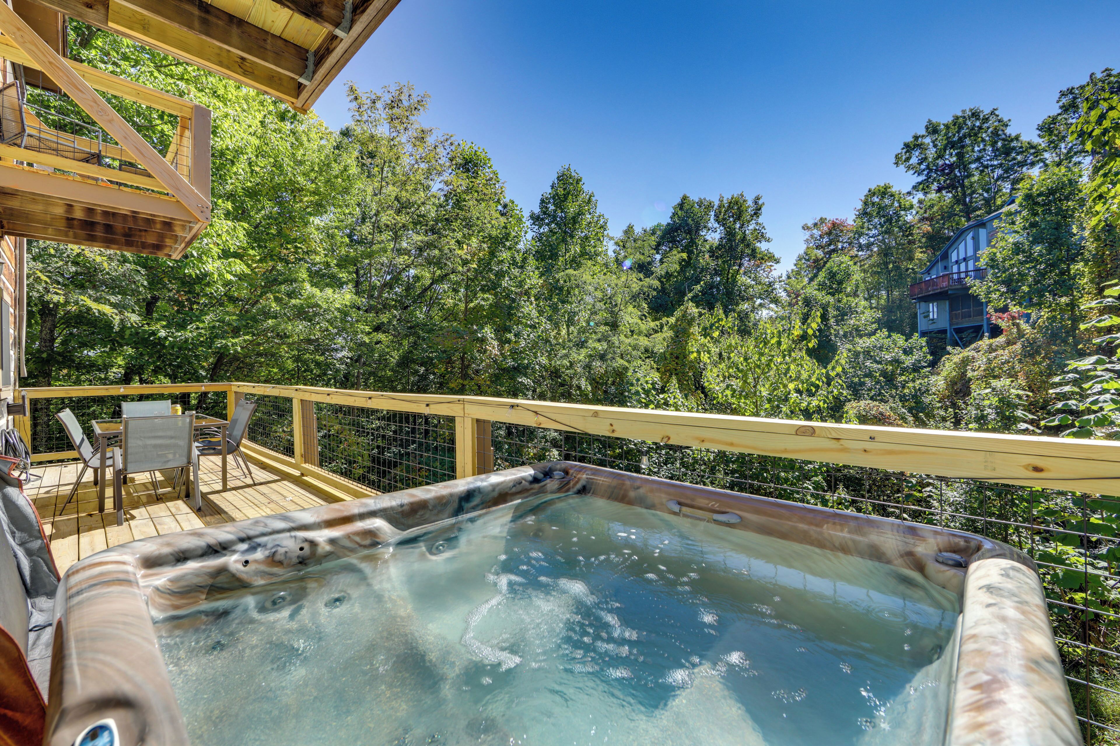 Uma banheira de hidromassagem em um deck de madeira com vista para uma área arborizada e uma casa ao fundo.