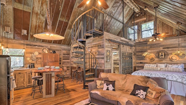 Interior rústico de uma cabana com área de jantar de madeira, um sofá e uma escada.