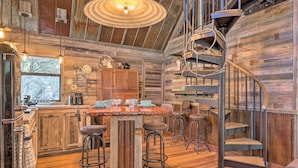Uma cozinha rústica com armários de madeira, um espaço de bar com banquetas e uma escada em espiral.