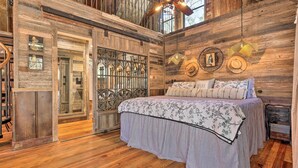 Quarto rústico com piso de madeira, cama com roupa de cama listrada, ventilador de teto e parede com objetos decorativos.