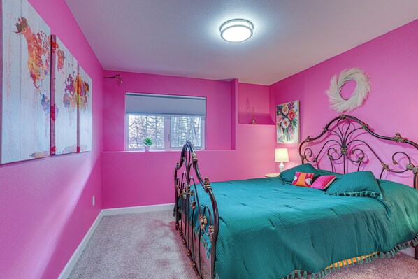 Quarto com paredes cor-de-rosa, colcha azul-turquesa e estrutura de cama de metal.