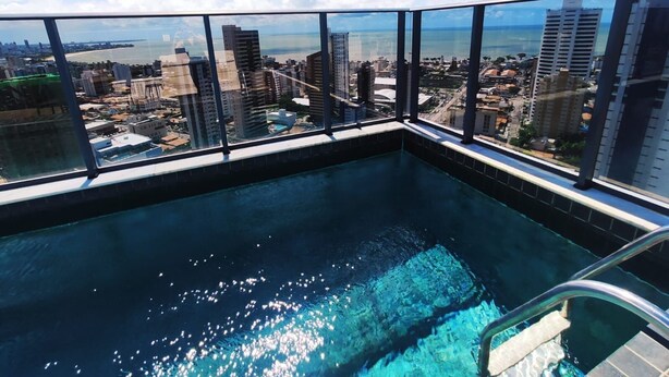 Piscina no terraço com vista para a cidade, cercada por edifícios altos.